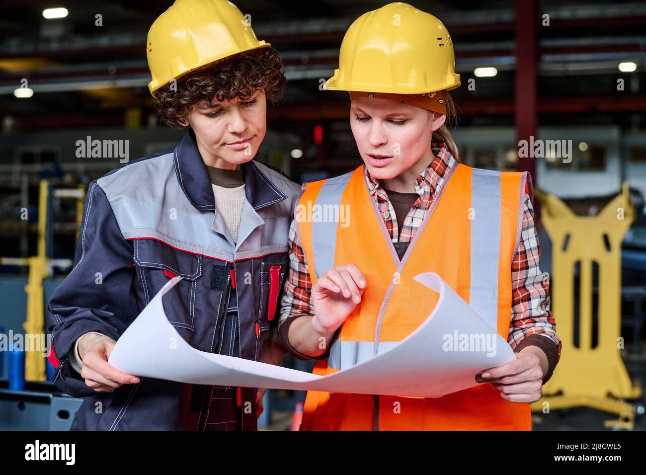 Two young female engineers discussing sketch on blueprint at working ...