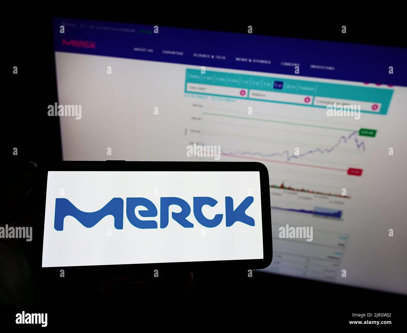 Person holding mobile phone with logo of German chemicals company Merck ...