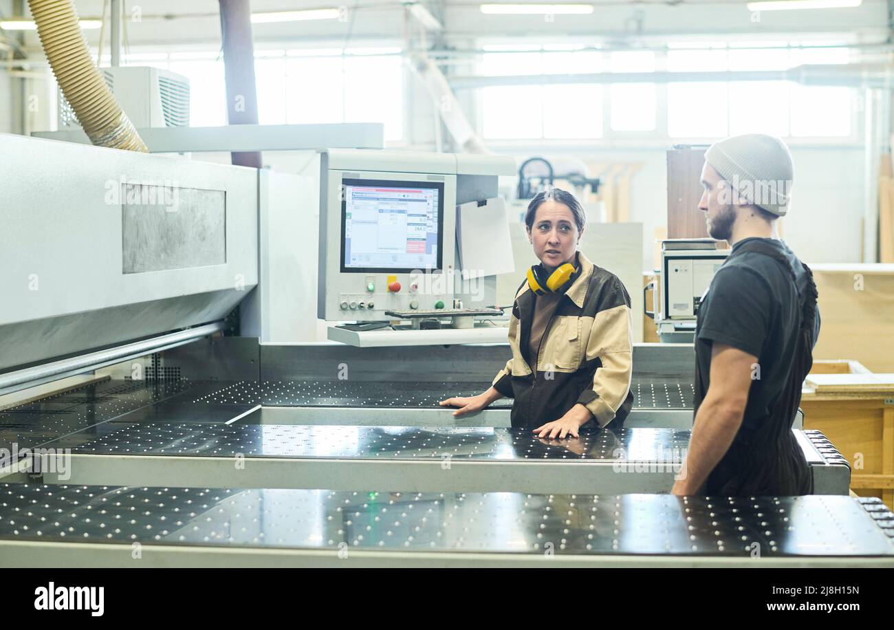Two colleagues standing at machine equipment and talking during work ...