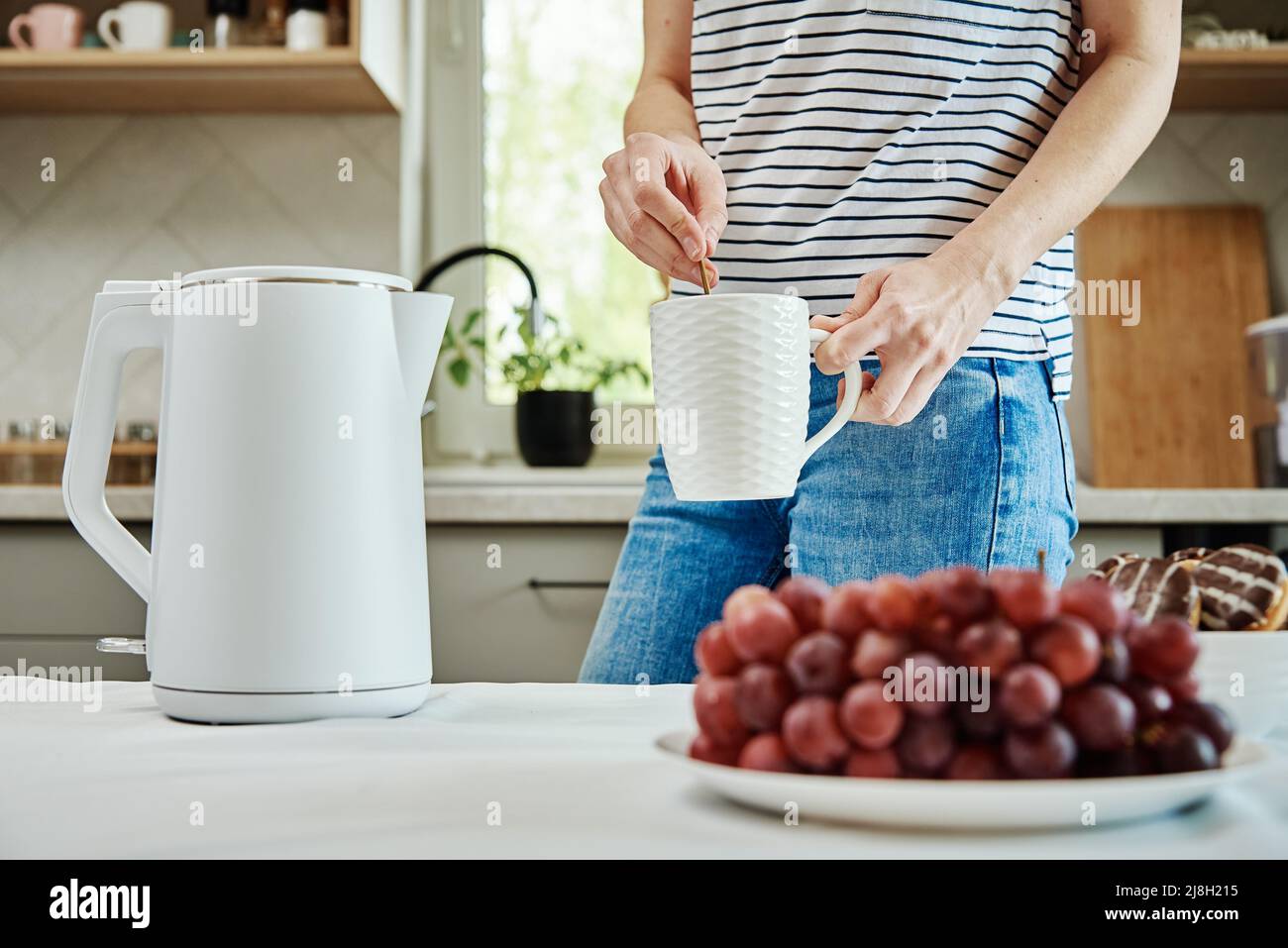Tea time, Woman pouring boiled water from electric kettle into cup for ...