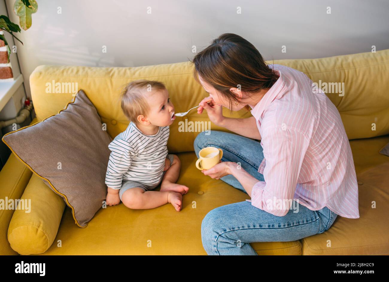 Mom feeds a small child at home with yogurt from a spoon. Family ...