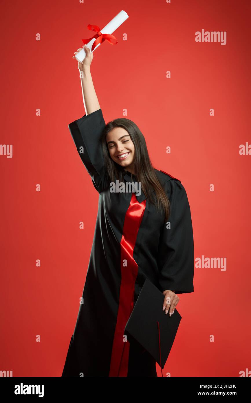Front view of girl in graduate gown standing, raising hand, holding ...
