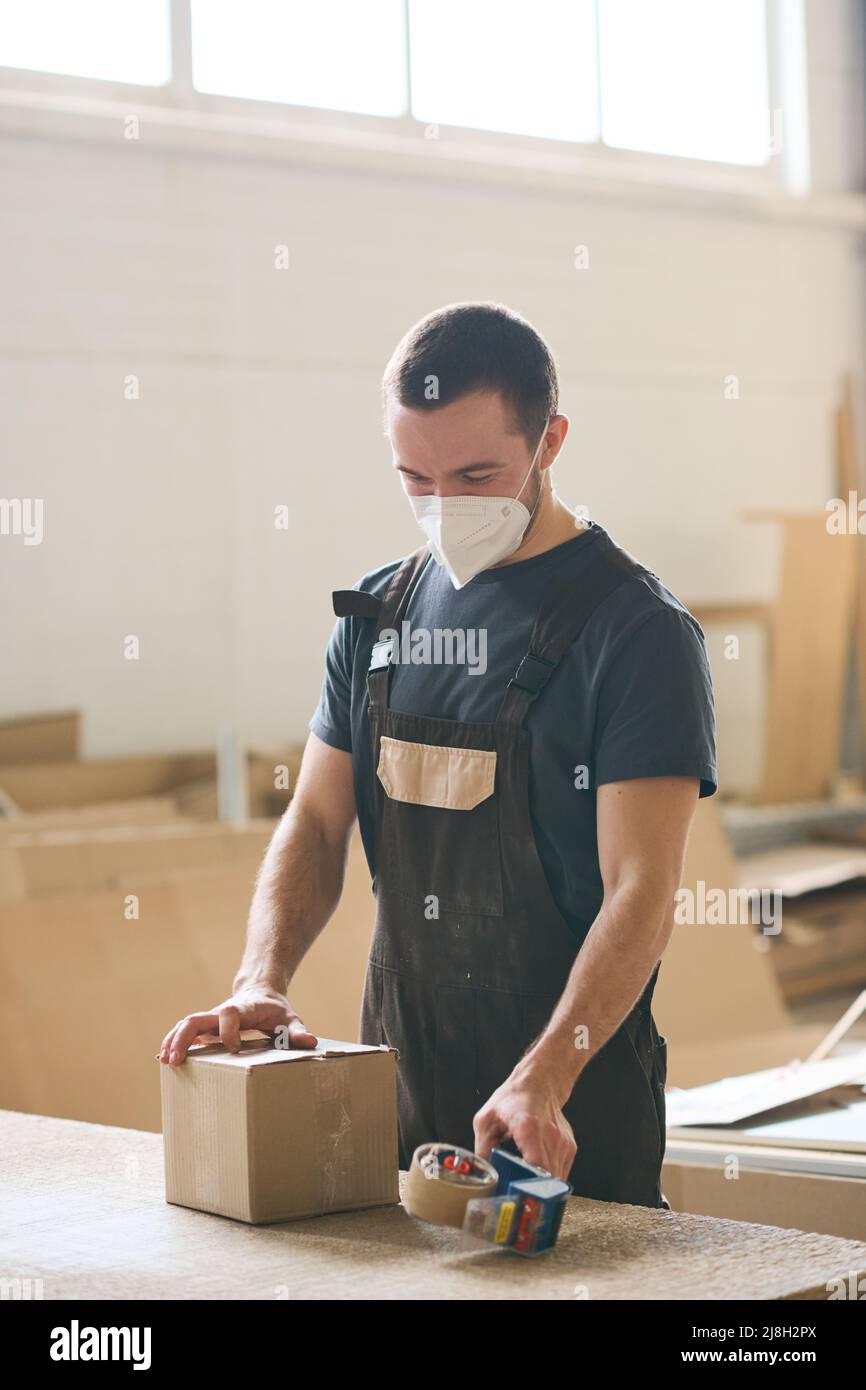 Young man in uniform standing at table and packing box with adhesive ...