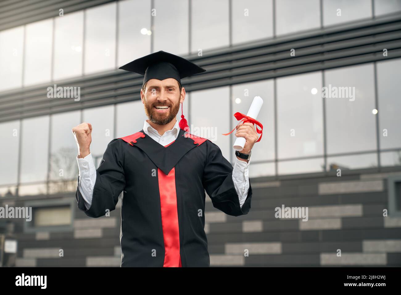 Front view of male student holding diploma, smiling, showing hurray ...