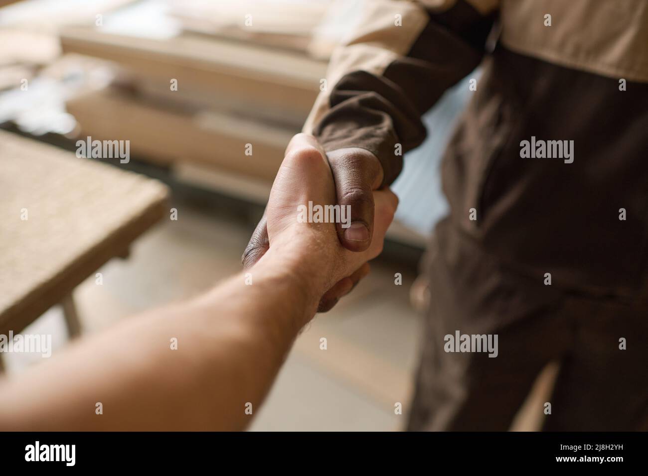 Close-up of two multiethnic manual workers shaking hands during ...