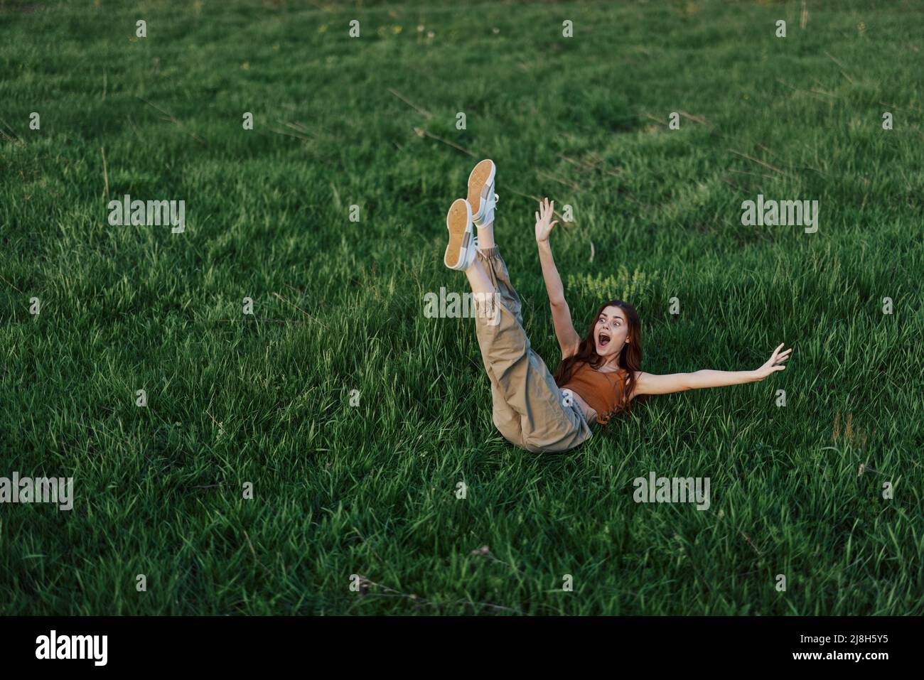 A Young Woman Playing Games In The Park On The Green Grass Spreading Her Arms And Legs In