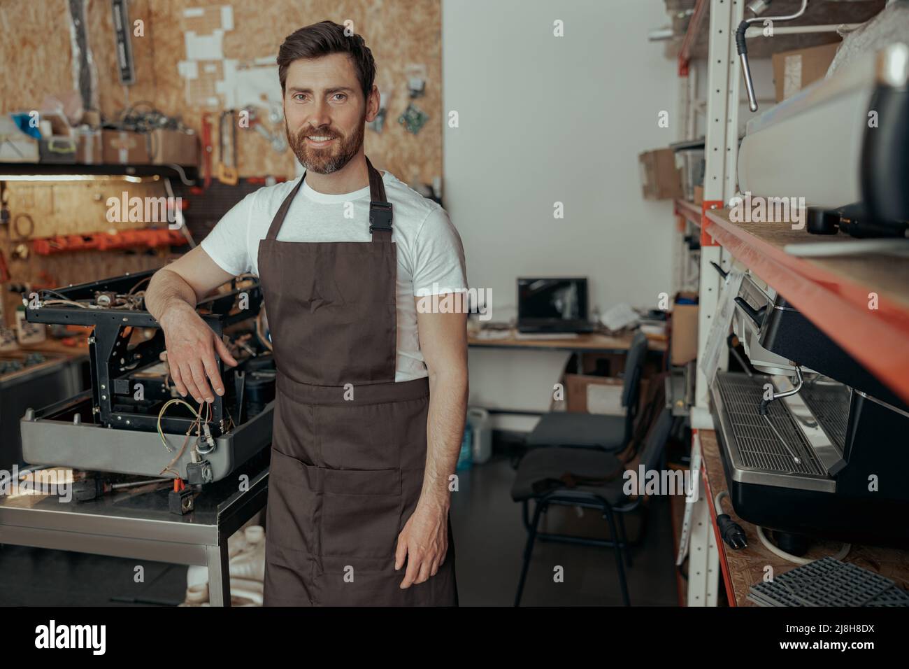 Portrait of repairman in uniform standing on workshop of coffee ...