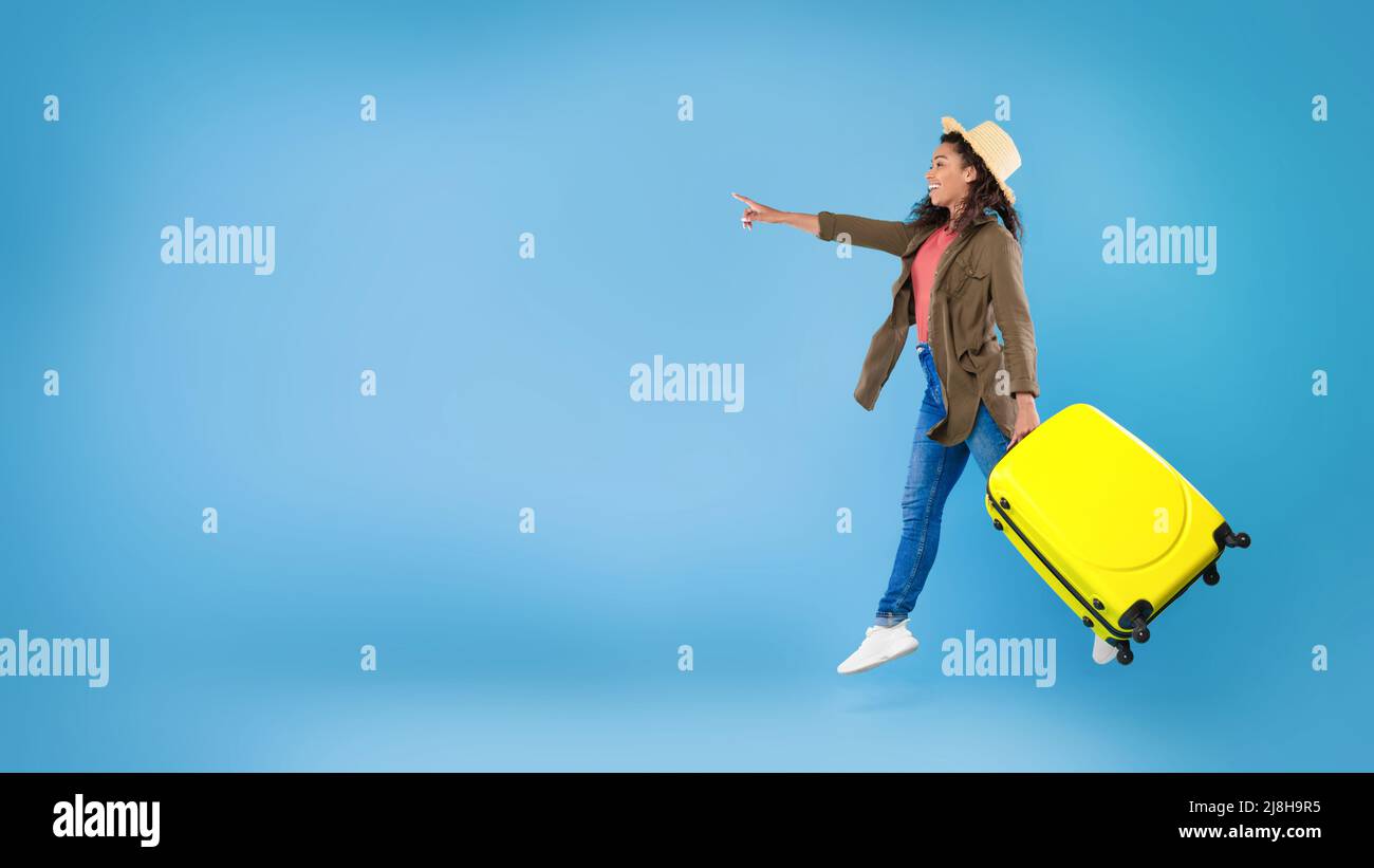 Cool young black lady running and jumping with bright suitcase ...