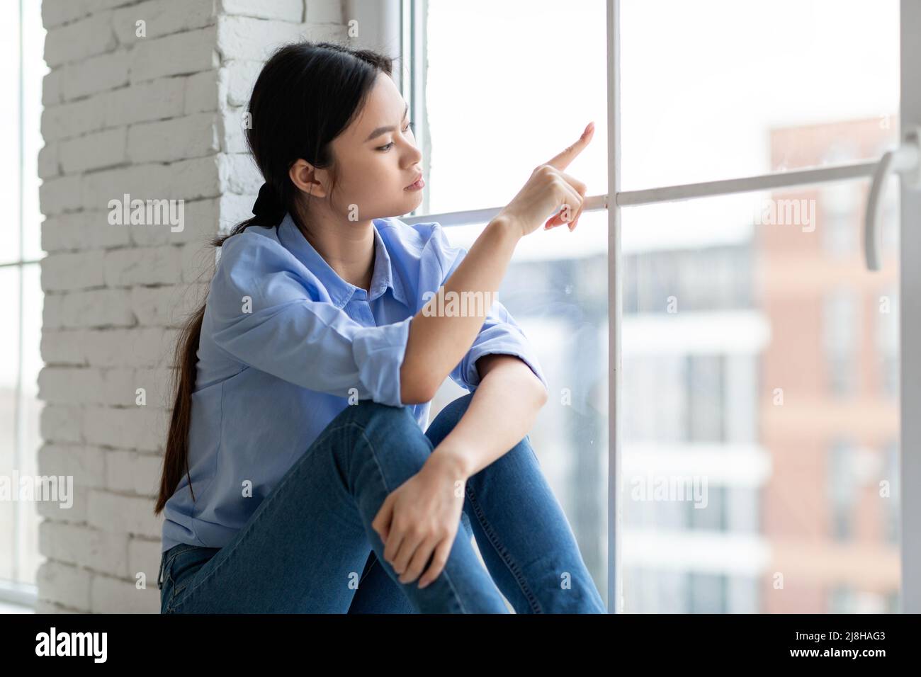 Upset millennial asian woman sitting on window at home Stock Photo - Alamy