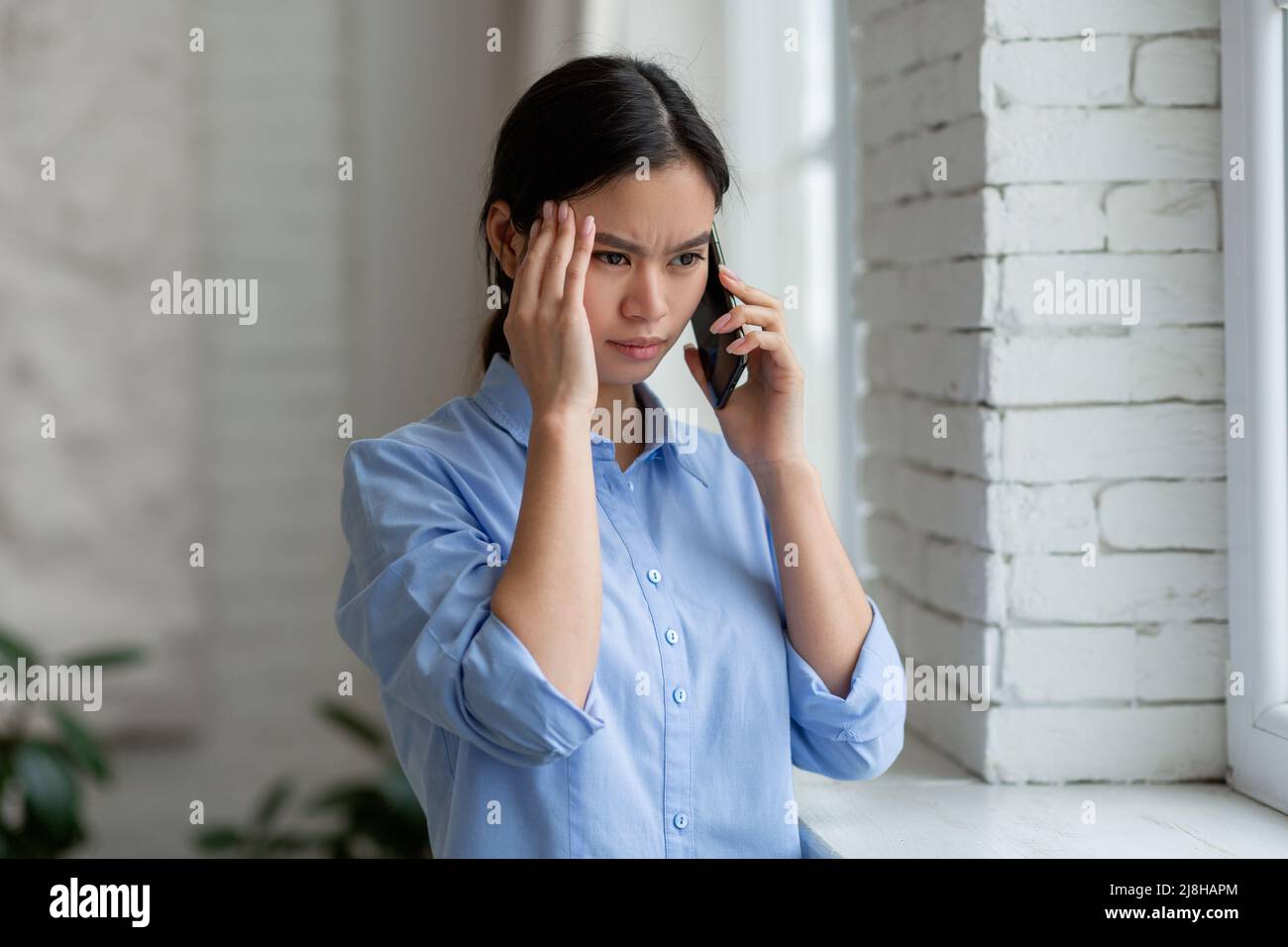 Upset asian woman standing by window, having phone conversation Stock ...