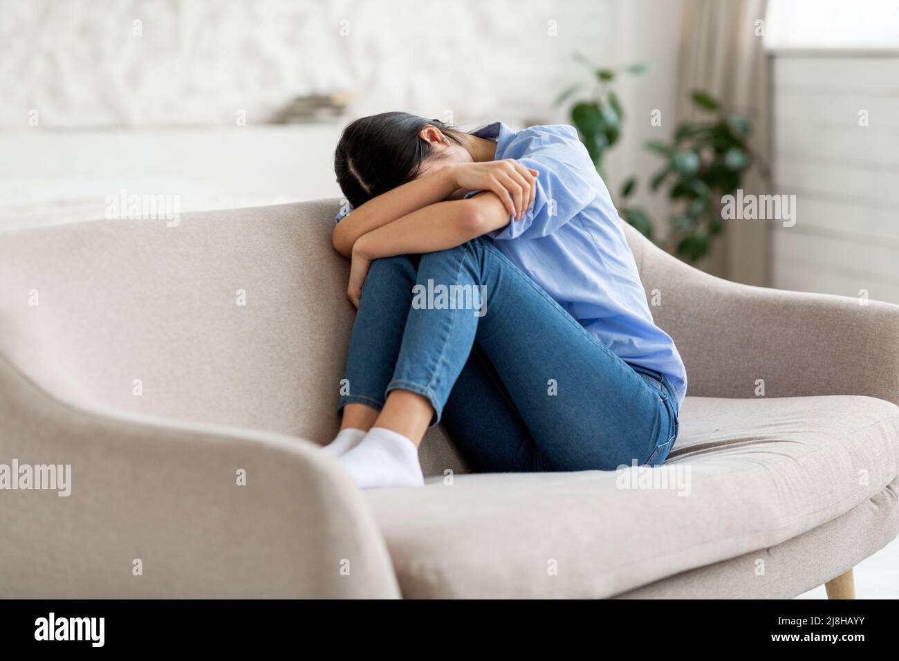 Side view of asian woman sitting on couch, crying Stock Photo - Alamy