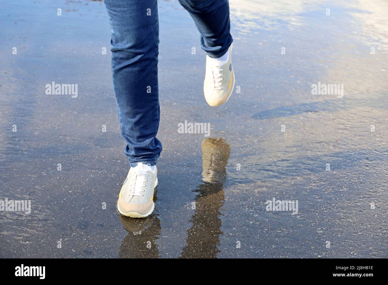 Female legs in jeans and sneakers on wet asphalt, woman run on a street ...