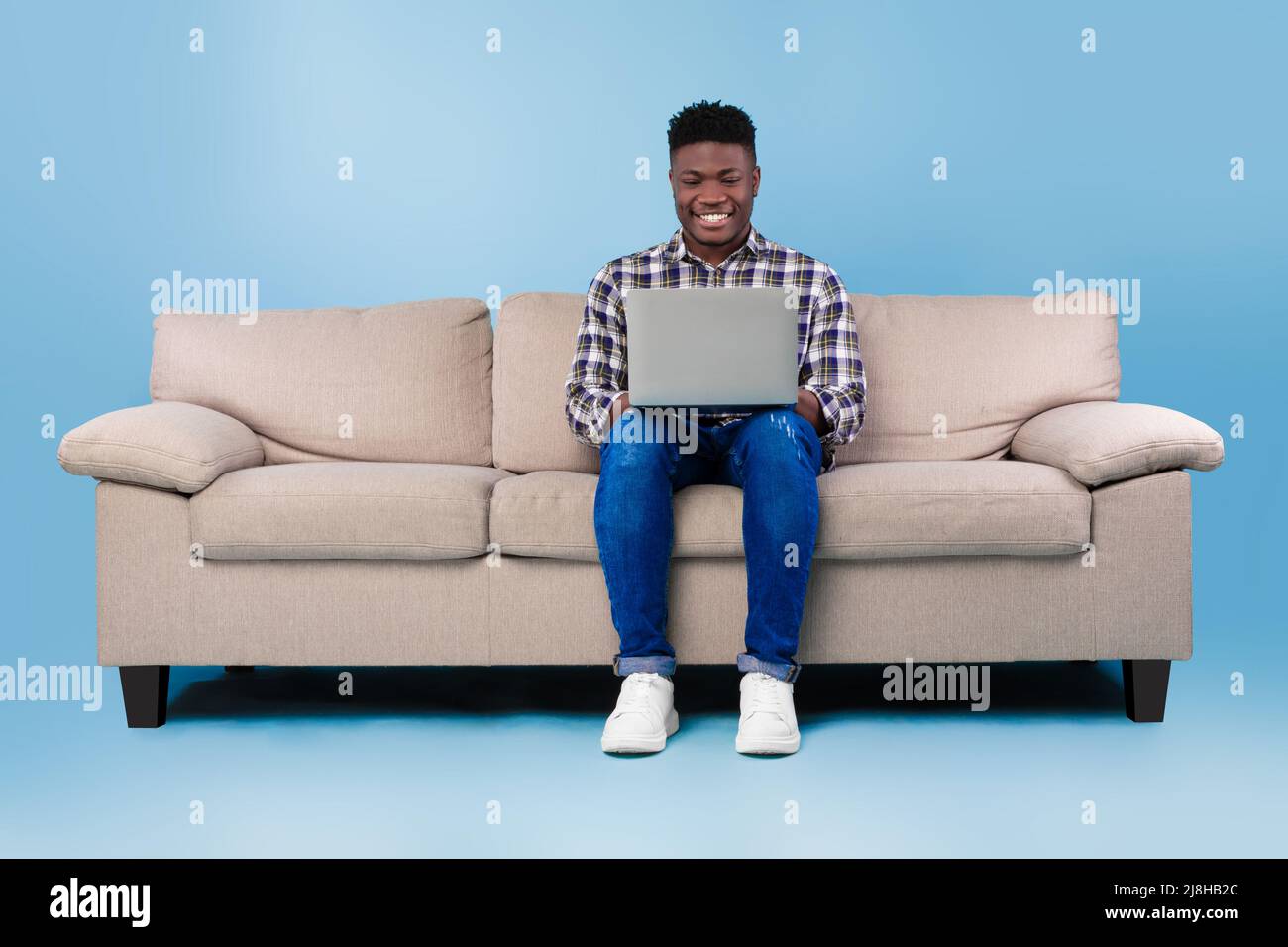 Cool young black guy sitting on sofa with laptop, working or studying ...