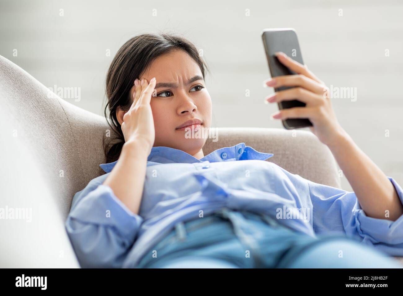 Closeup of chinese woman suffering from headache, using smartphone ...