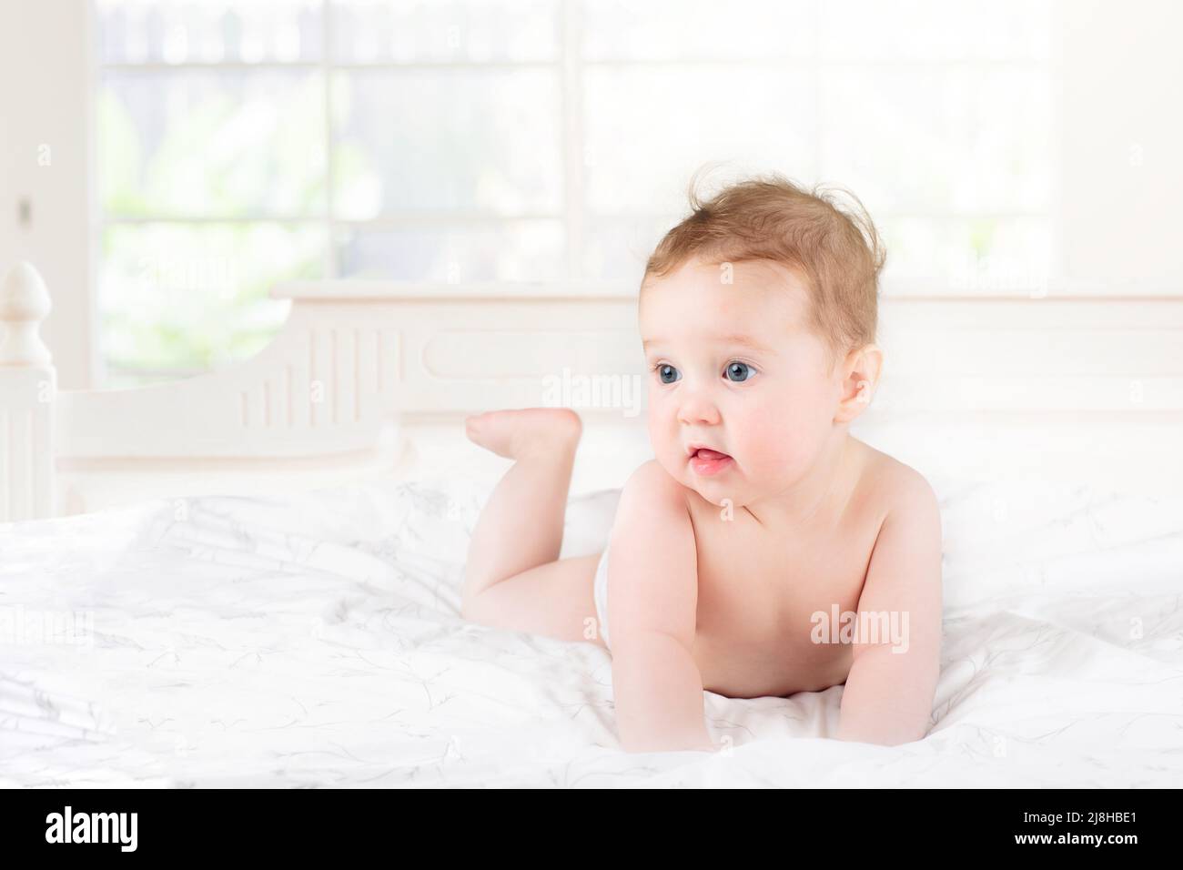 Baby in diaper crawling on bed. Little child playing in white sunny ...
