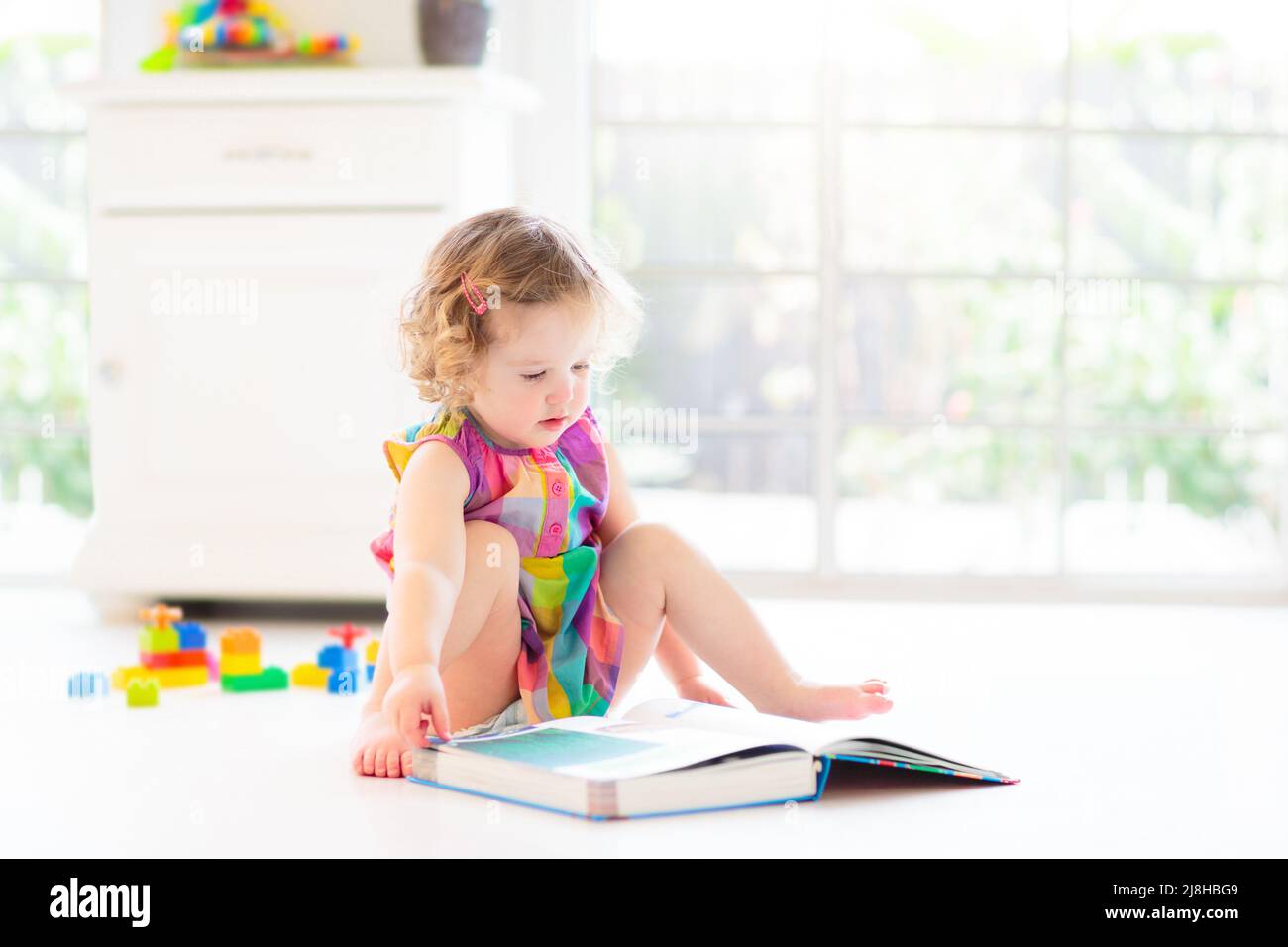 Child reading book in white sunny bedroom with big window. Children ...