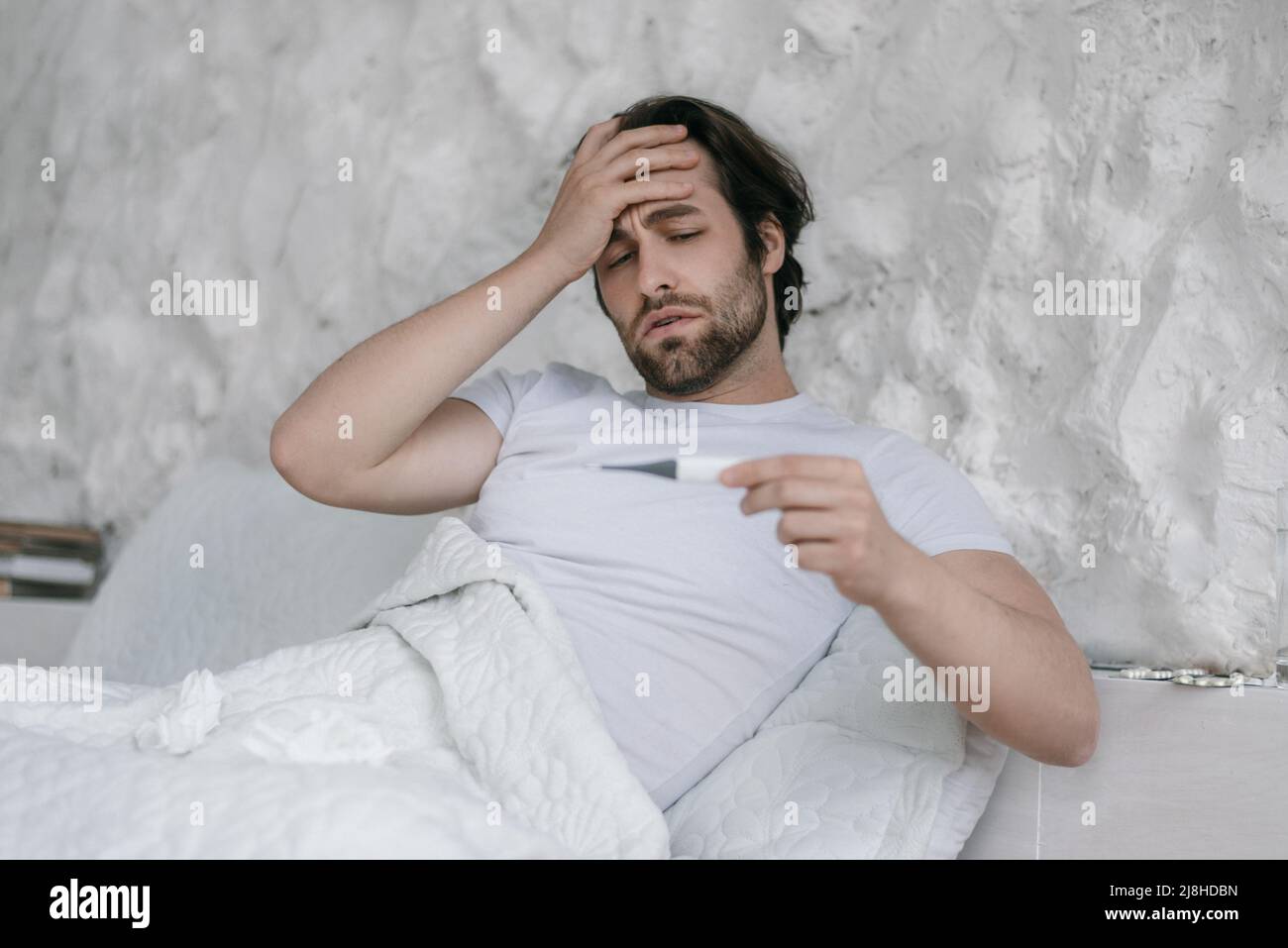 Despaired Millennial Caucasian Guy With Stubble On Bed Touches