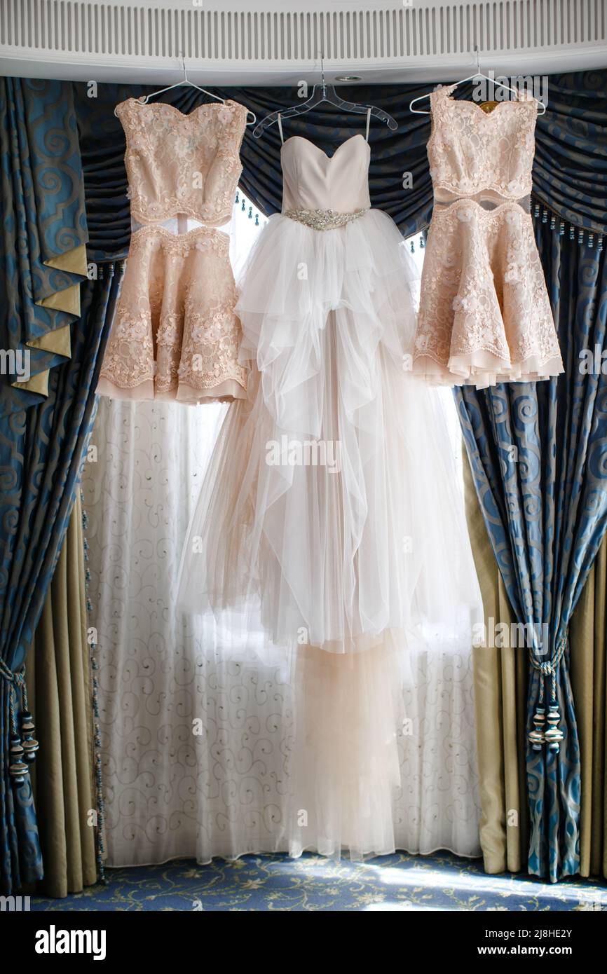 Wedding and bridesmaids dresses hanging by the window Stock Photo - Alamy