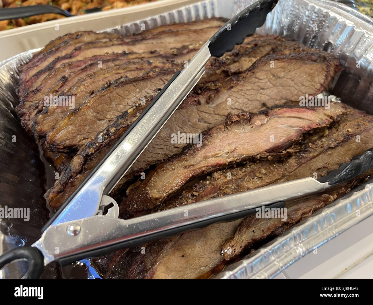 Tongs are visible atop a chafing dish of smoked beef brisket strips ...