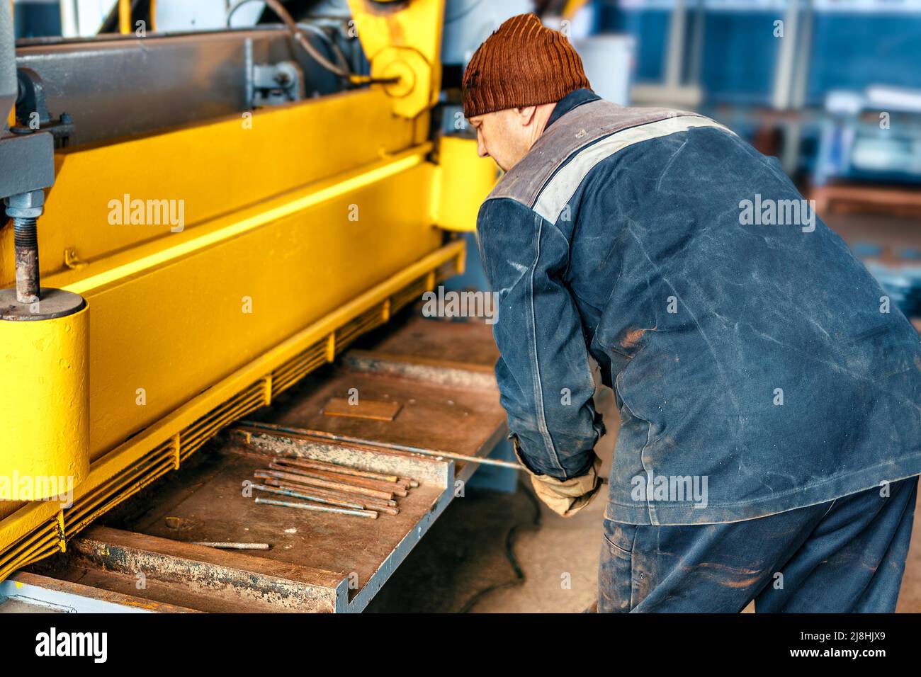 Worker cuts metal on mechanical guillotine machine in production hall ...