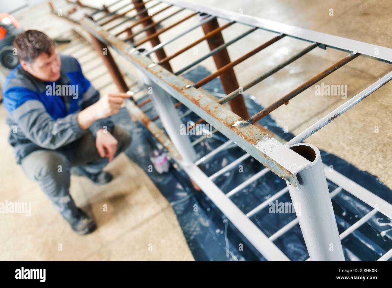 Caucasian worker in overalls paints metal rack or ladder with paint ...