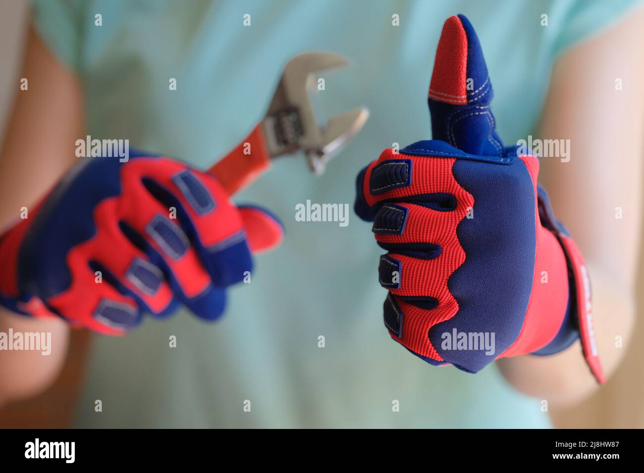 Female hands in work gloves holding wrench and showing thumb up gesture ...