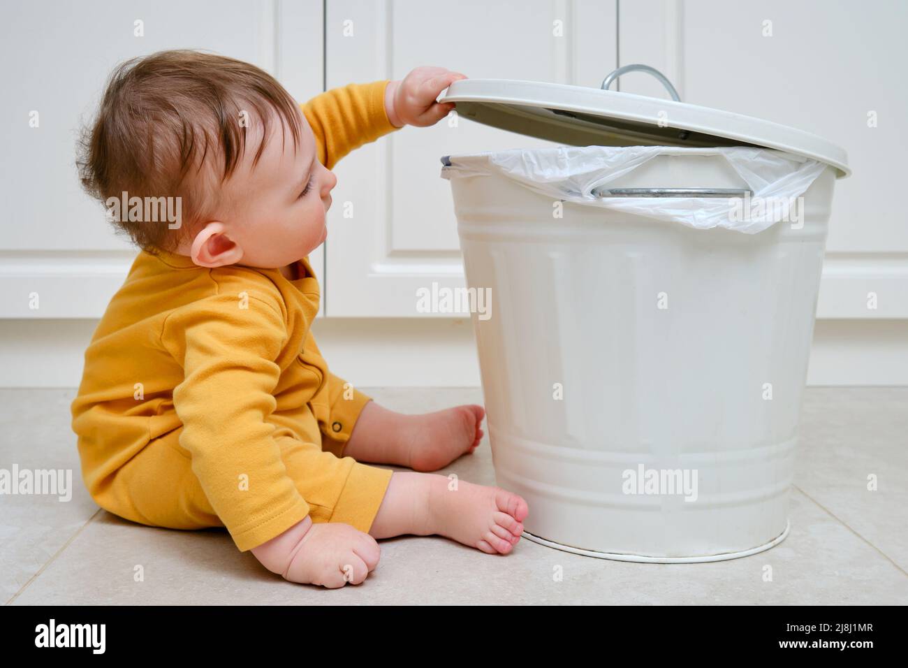 Toddler baby boy opens a trash can with household waste. Children's ...
