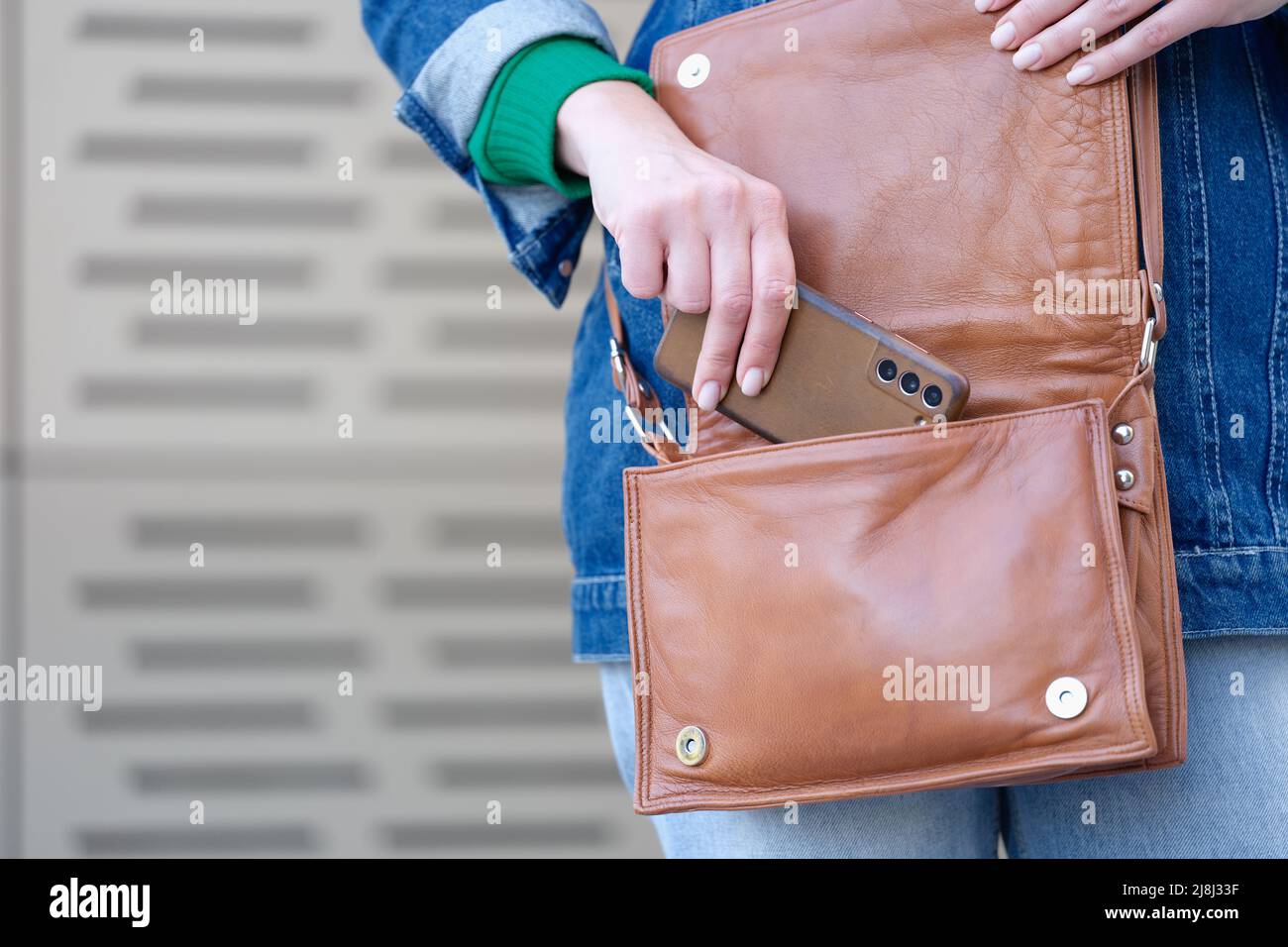 Young woman putting modern smartphone in bag Stock Photo - Alamy