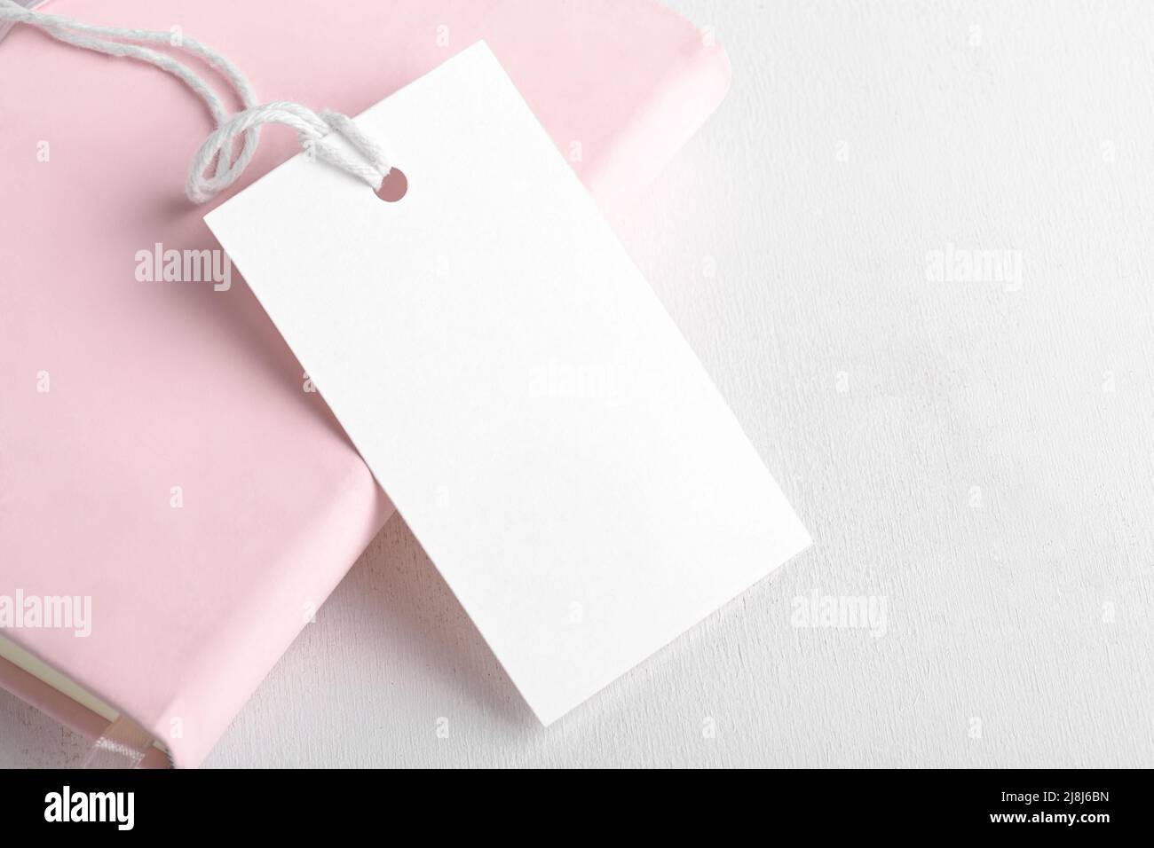 Rectangle white gift tag mockup with white cord, close up on pink book ...