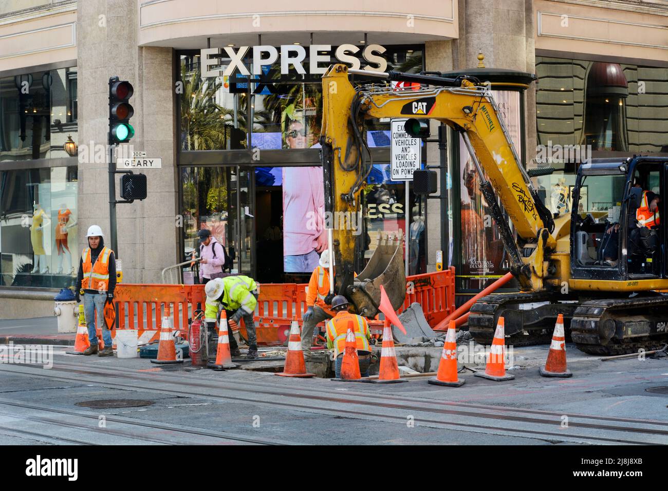 A crew makes underground utility and road repairs at a busy street ...