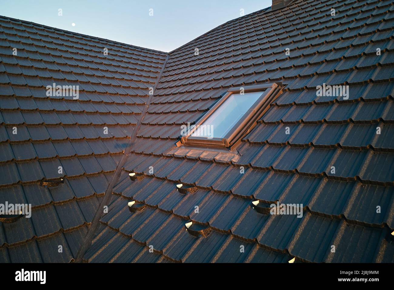 Closeup of attic window on house roof top covered with ceramic shingles ...