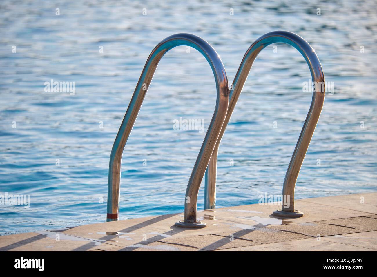 Close up of swimming pool stainless steel handrail descending into ...