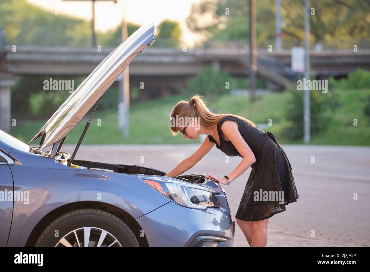 Helpless woman standing near her car with open bonnet inspecting broken ...