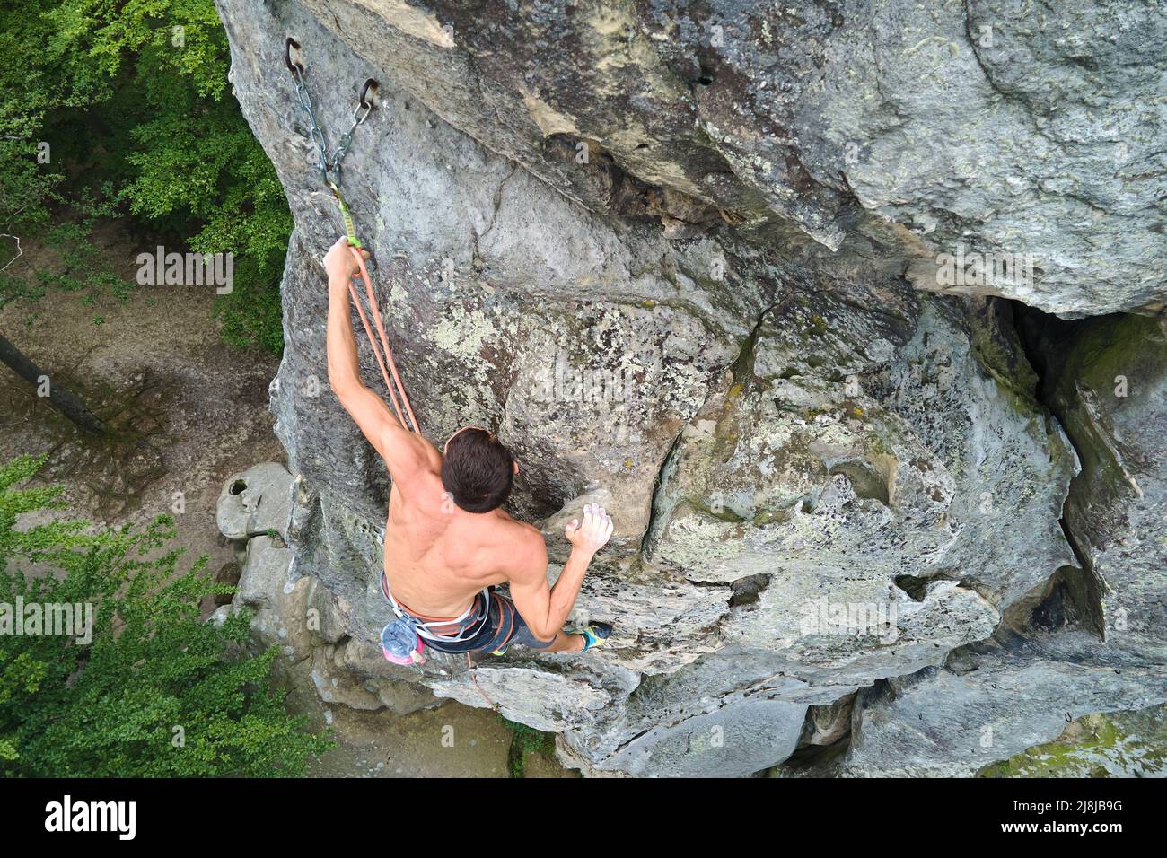 Young man climbing steep wall of rocky mountain. Male climber overcomes ...