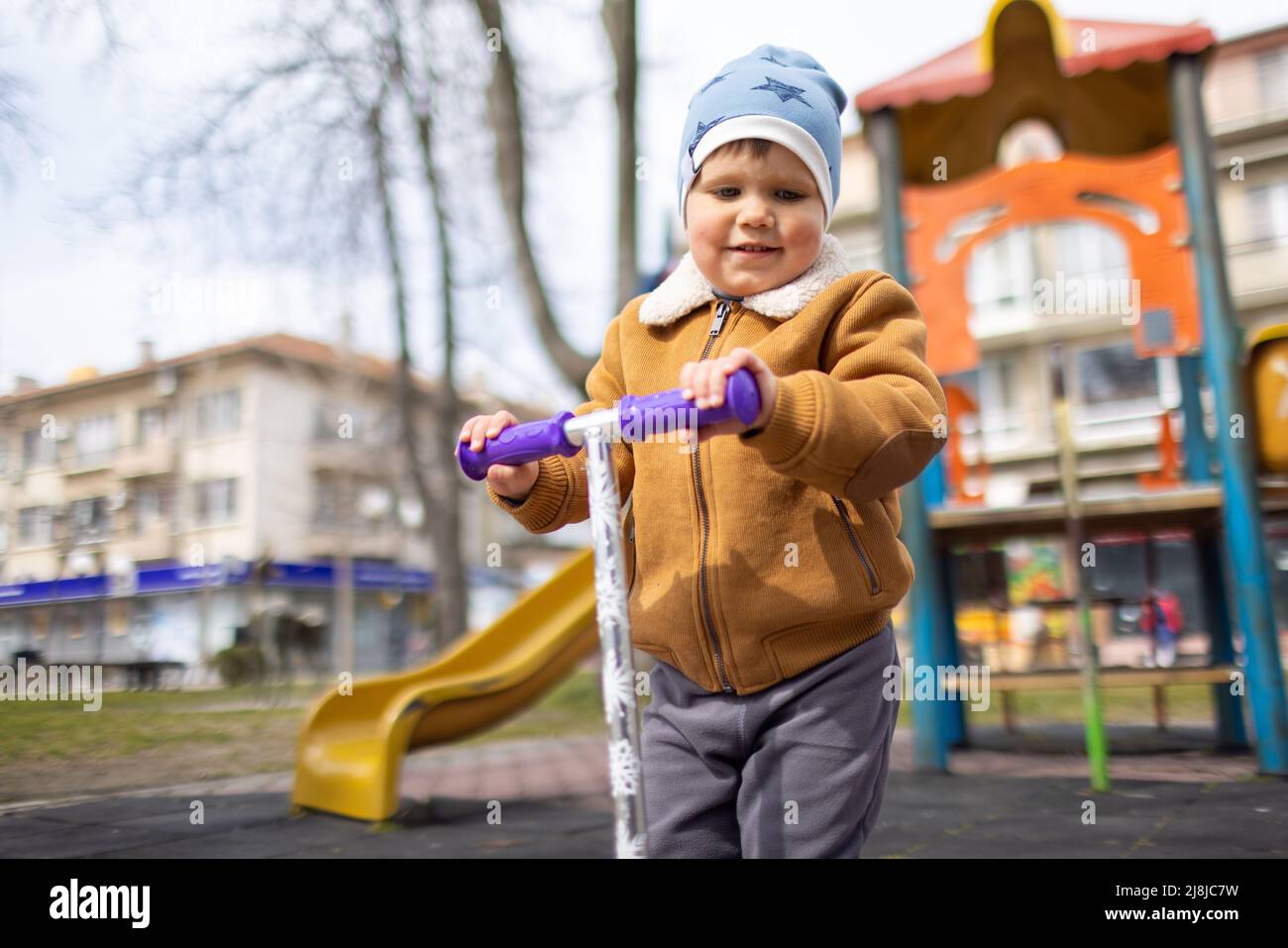 An active little cheerful boy in a blue cap and warm clothes plays on ...
