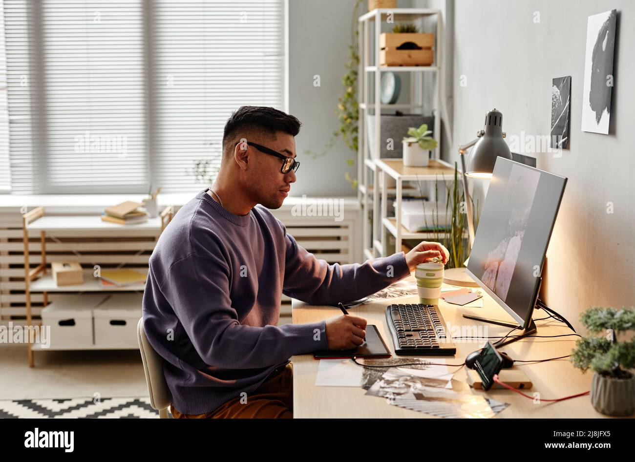 Side view portrait of Asian male creator editing photographs at home ...