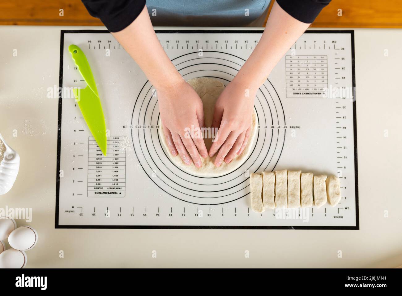 Top view of hands kneading rolled out dough on a kitchen baking mat with round markings of ...