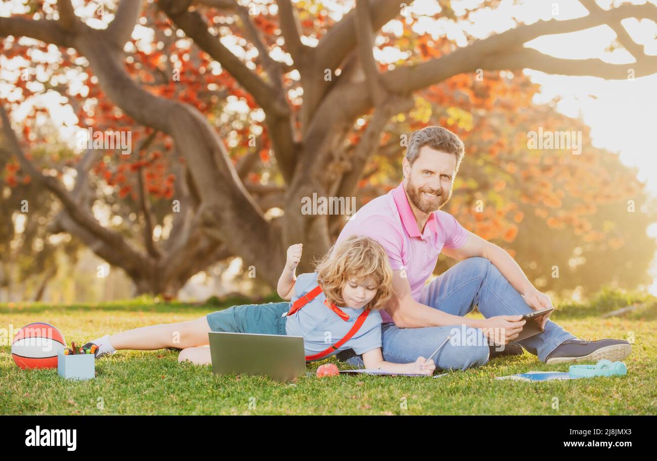 Outdoor learning. Father and son playing or studying with laptop in the ...