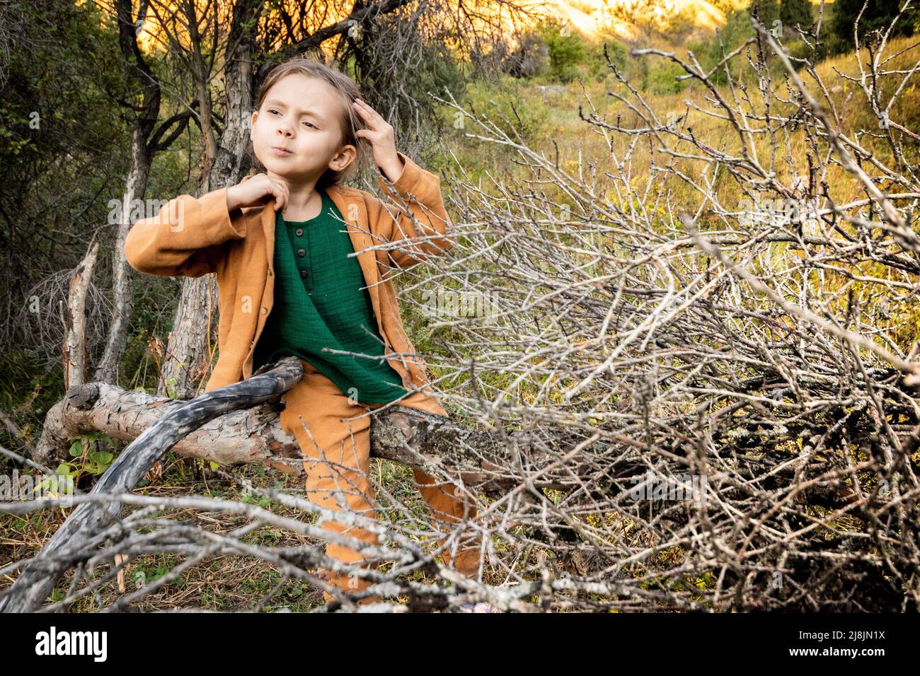 Girl 5 - 7 years old sits on a branch of a fallen tree during outdoor ...