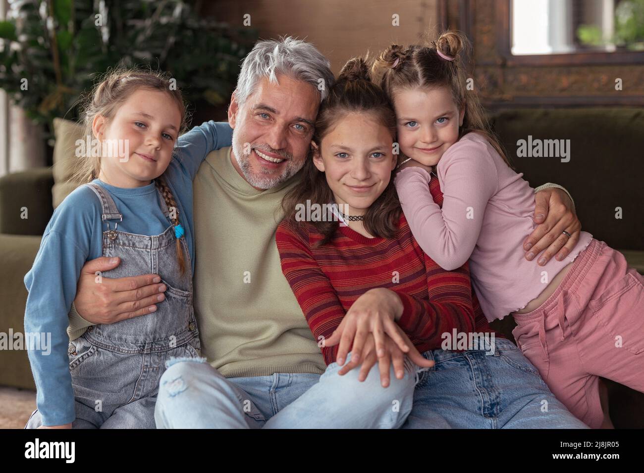 Portrait of three little daughters hugging their happy father at home ...