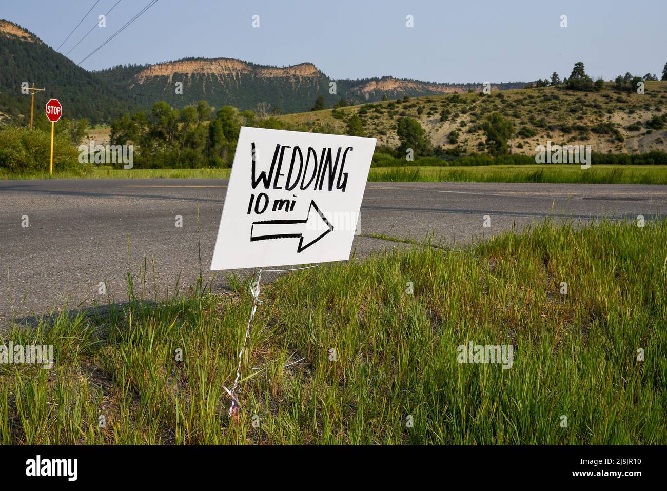 A handmade white sign with an arrow that reads Wedding 10 miles, a red ...