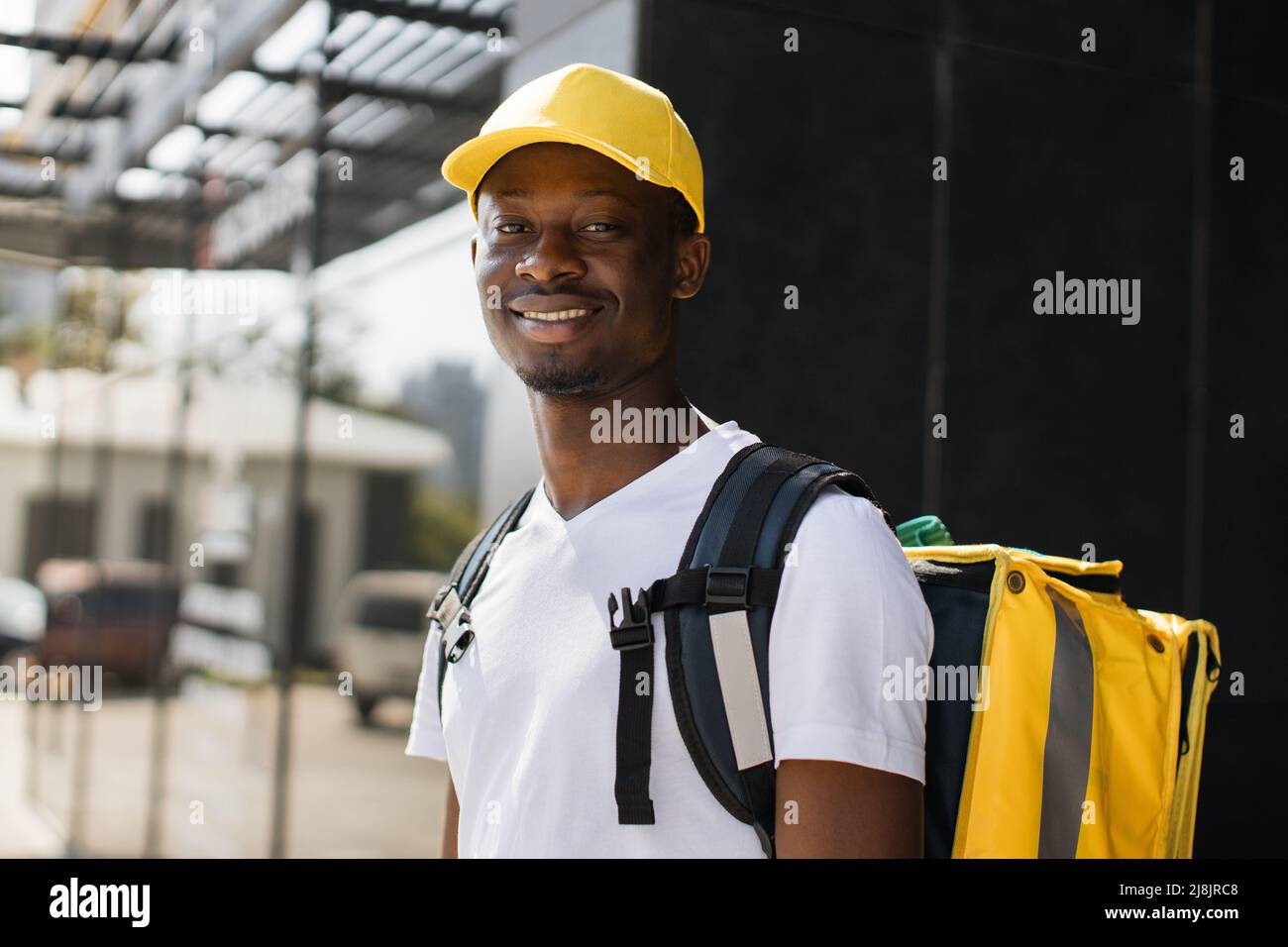 Portrait of delivery man with yellow cap and thermal backpack looking ...