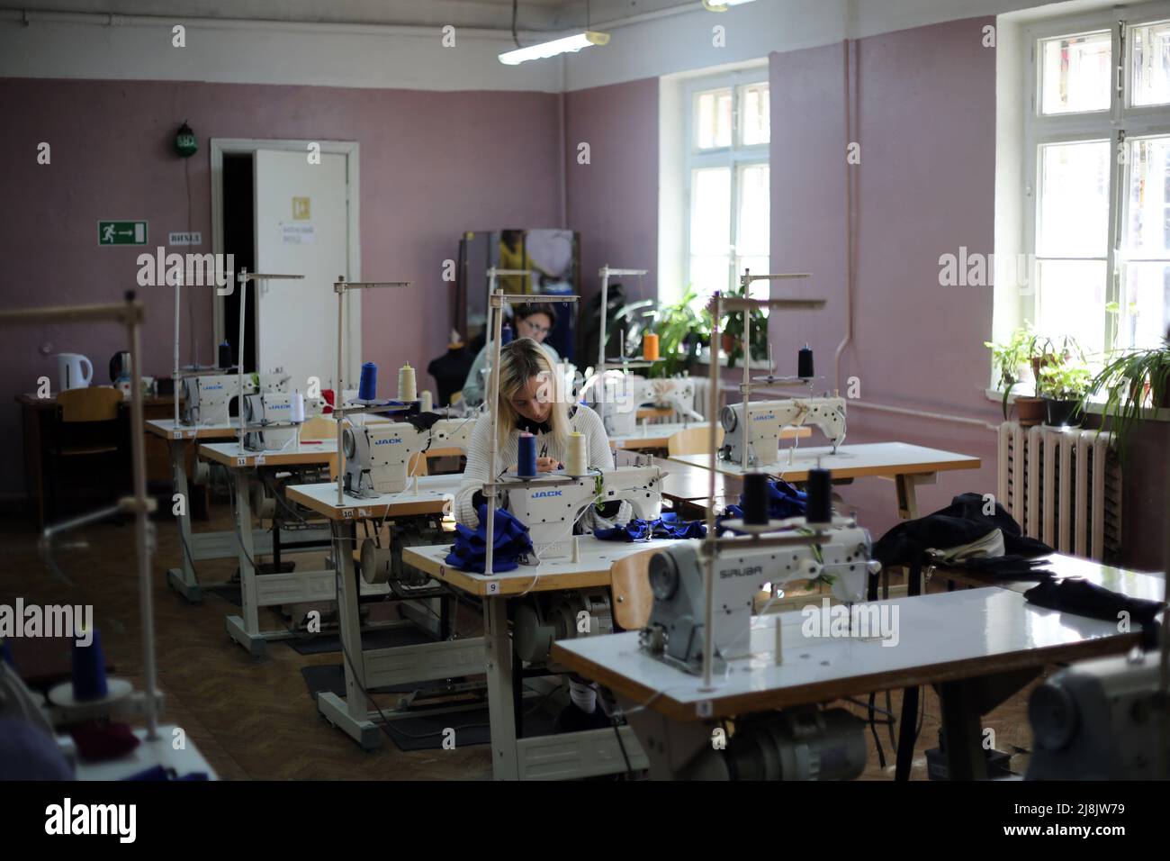 A young seamstress volunteer sews material on a sewing machine to make ...