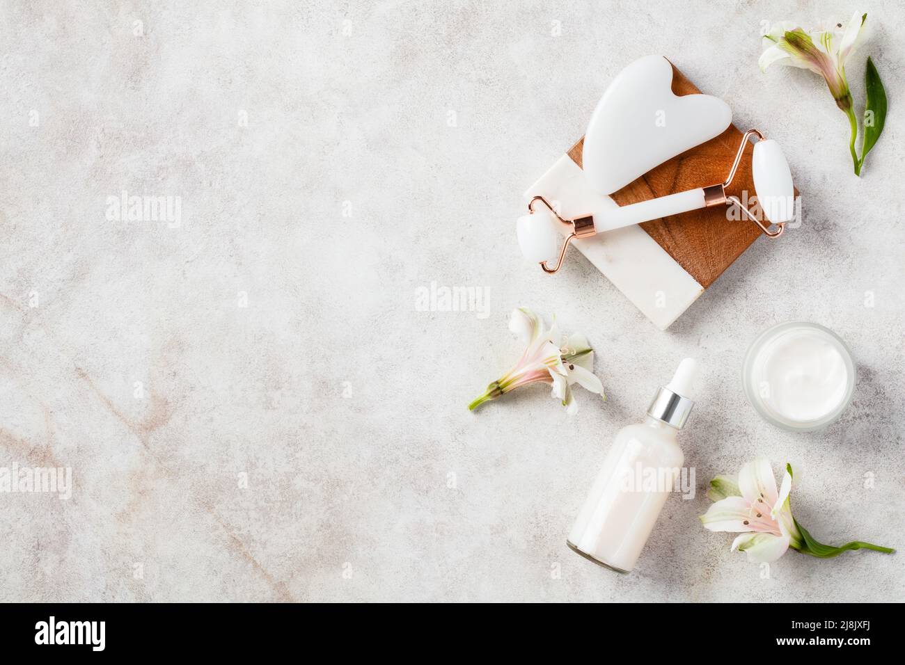 Flat lay white jade face roller, gua sha, serum, moisturizer cream ...