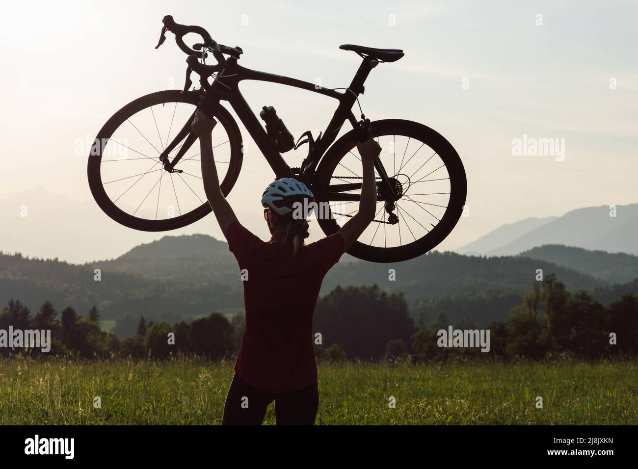 Female road cyclist raising bicycle with both arms above her head at ...