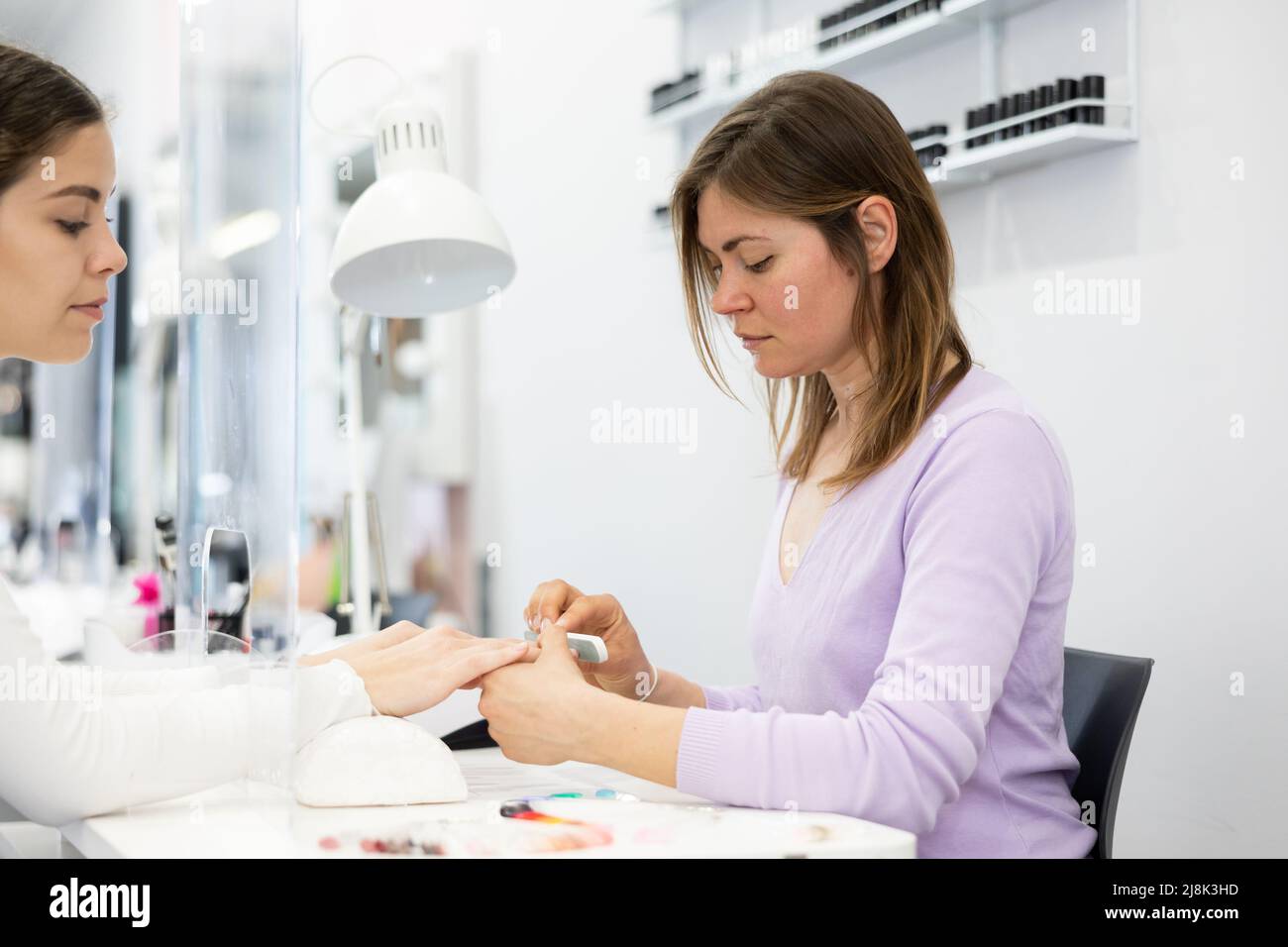 Manicurist files the nails of a young female client Stock Photo - Alamy