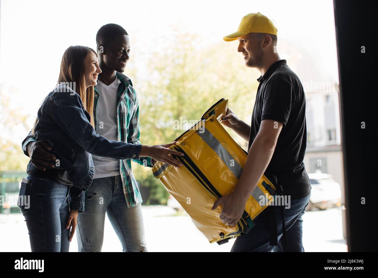Courier delivering parcel for multinational couple at the door of their ...
