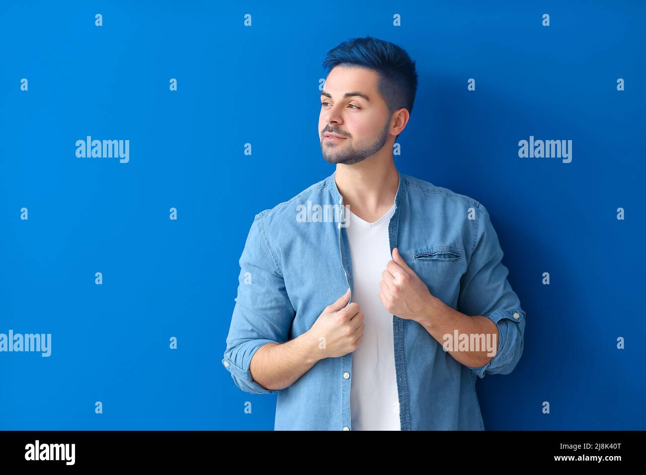 Stylish young man with unusual blue hair and beard on color background ...