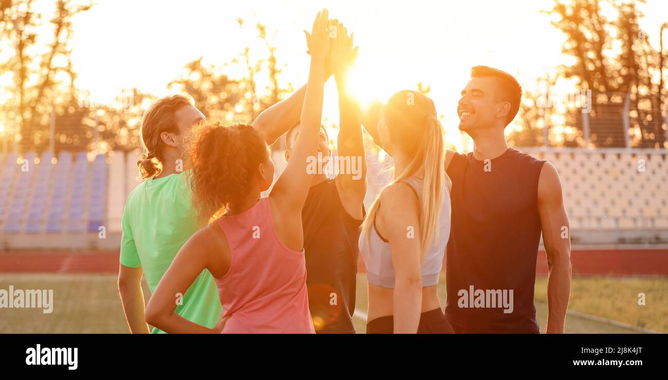 Group of sporty young people putting hands together at the stadium ...