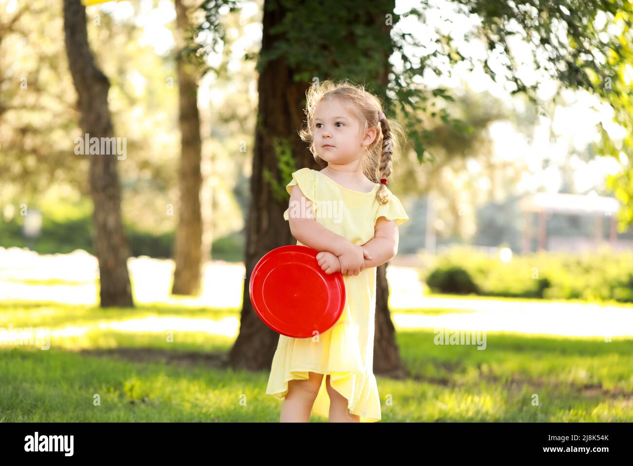 Cute little girl in yellow dress playing frisbee in park Stock Photo ...